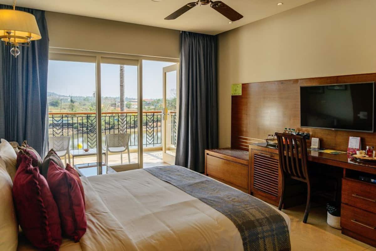 Quarto de hotel com uma cama grande, uma escrivaninha com cadeira, televisão e varanda com vista para a paisagem.