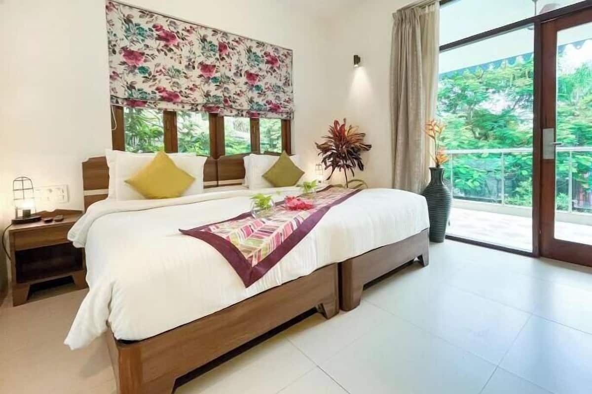 Quarto de hotel com uma cama grande, uma mesa de cabeceira, uma janela com cortinas e vista para o verde lá fora.