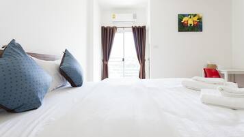 Quarto de hotel com uma cama grande, roupa de cama branca, almofadas azuis, uma cadeira vermelha e um quadro na parede.