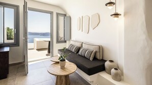 Sala de estar moderna com sofá, mesa redonda de madeira com uma planta e vista para o mar através de grandes janelas.