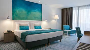 Quarto de hotel moderno com uma cama grande, uma escrivaninha, uma cadeira e vista para o exterior.