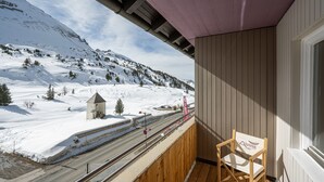 Varanda de madeira com uma cadeira, com vista para uma paisagem montanhosa coberta de neve e um teleférico.