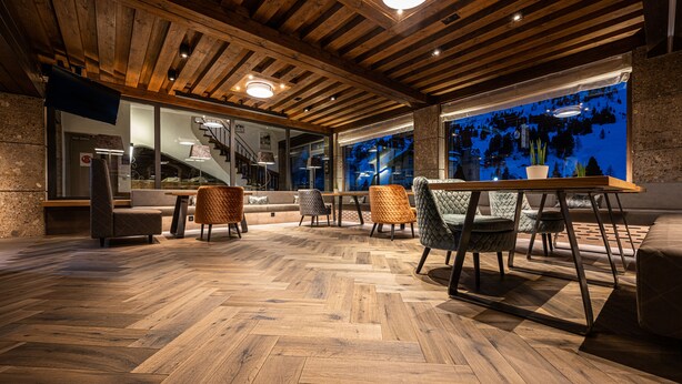 Quarto espaçoso com piso de madeira em padrão herringbone, uma janela grande com vista para árvores e design de interiores moderno.