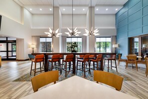 Um lobby moderno de hotel com área de bar, assentos e amplas janelas.