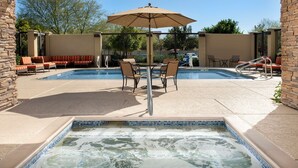 Piscina com hidromassagem, rodeada por espreguiçadeiras e uma mesa com guarda-sol.