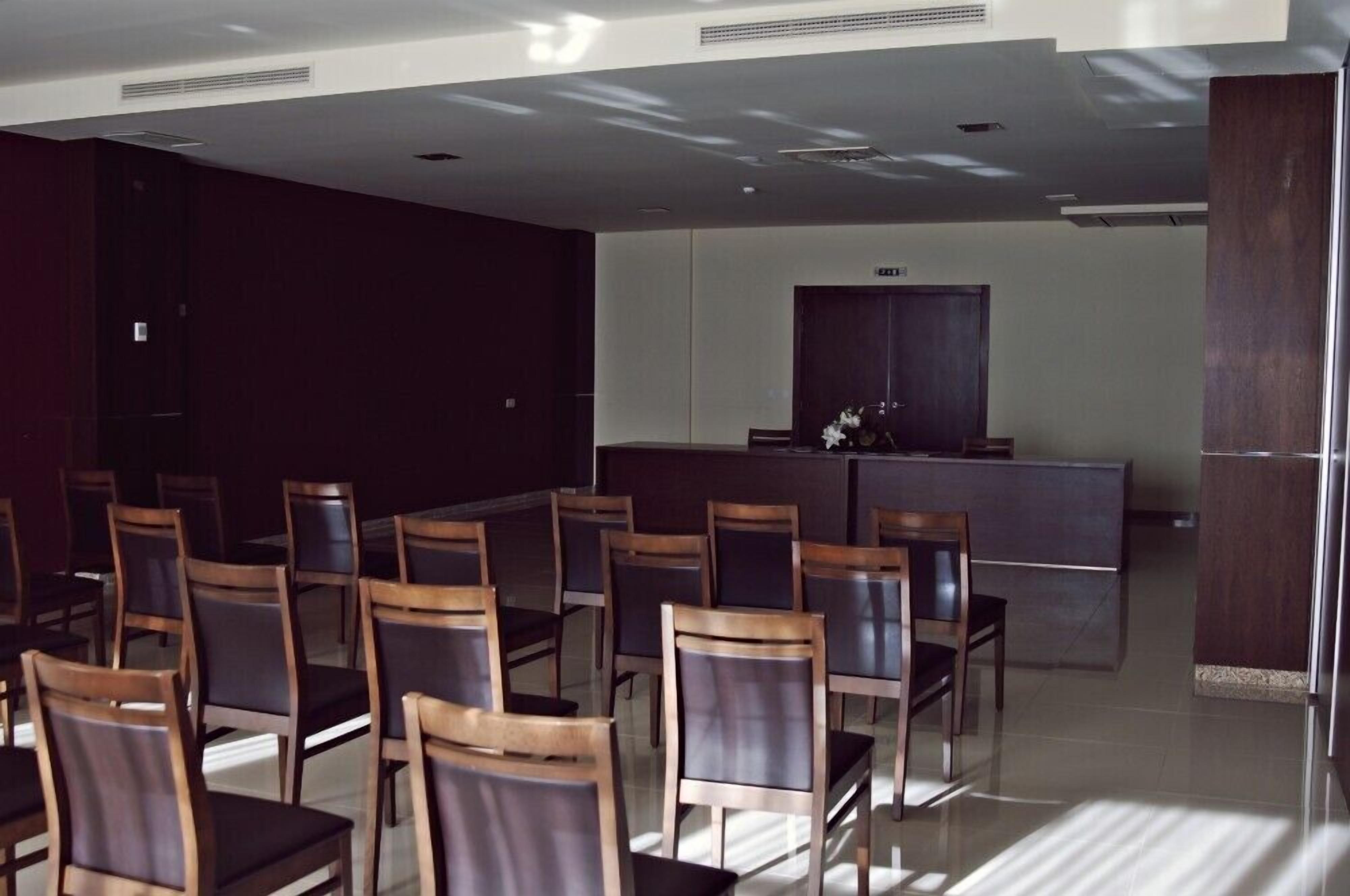 Uma sala de conferências com fileiras de cadeiras, um balcão de recepção e uma janela grande.