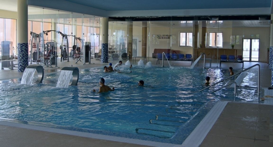Piscina interior com várias pistas de natação, equipamentos de ginástica e área de estar.