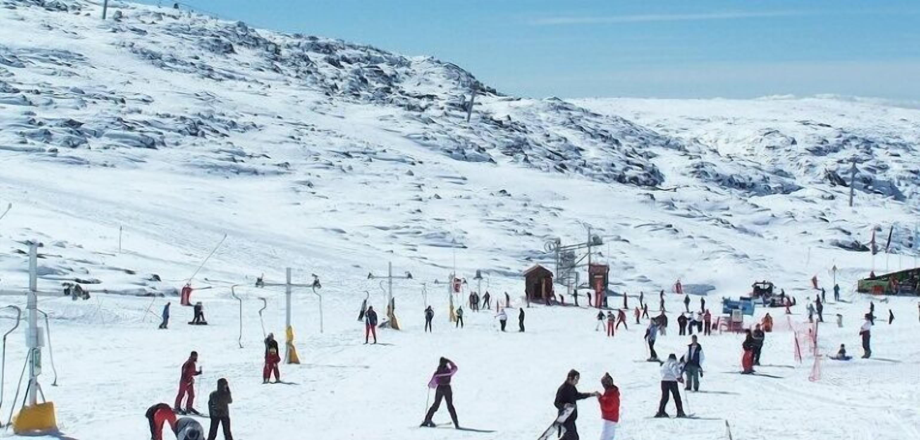 Pista de esqui coberta de neve, com esquiadores e um teleférico.