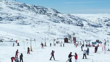 Pista de esqui coberta de neve, com esquiadores e um teleférico.