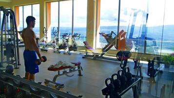 Uma academia com amplas janelas, equipamentos de ginástica e vista para o oceano.