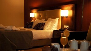 Quarto de hotel com cama, luminárias de cabeceira, mesa de apoio, espelho e preparação para o café da manhã, incluindo um copo de suco de laranja e duas canecas.