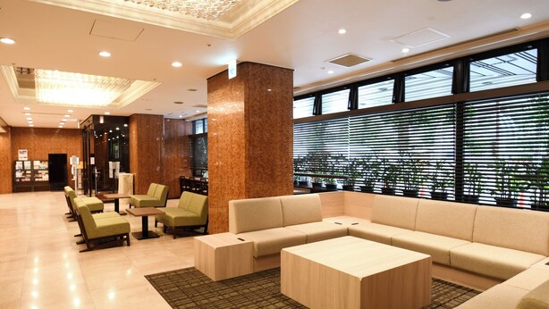 Um lobby moderno com um amplo sofá em forma de L, cadeiras verdes e uma mesa de centro.