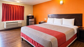 Quarto de hotel com uma cama, aquecedor, micro-ondas e telefone em uma mesinha de cabeceira.