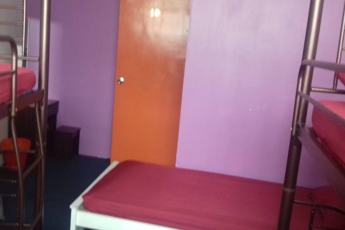 Quarto com beliches, uma porta e parede roxa.