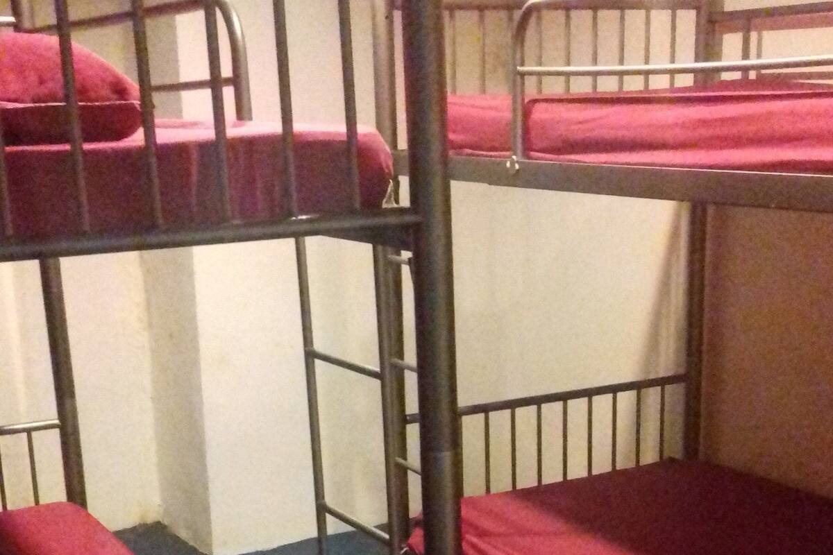 Quarto com beliches, grades de metal e roupa de cama vermelha.