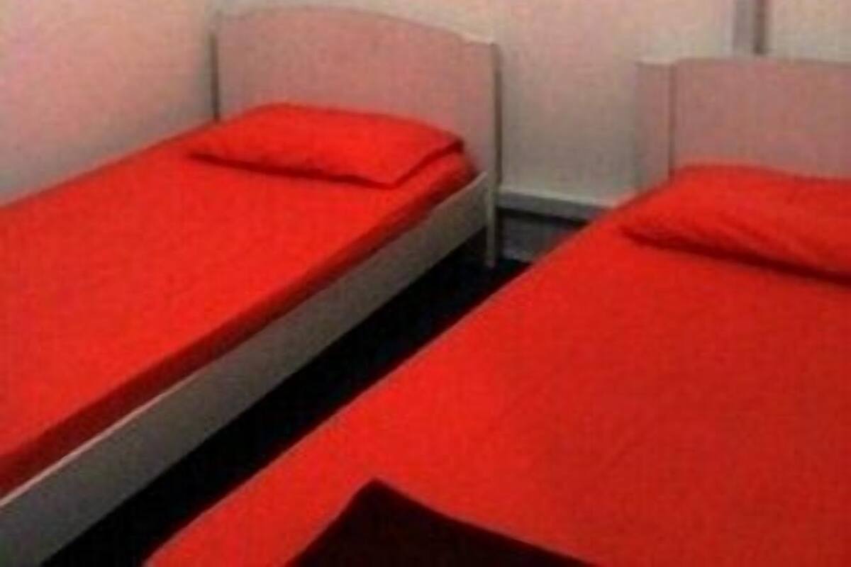 Quarto pequeno e individual com duas camas de solteiro, cada uma com colcha vermelha.