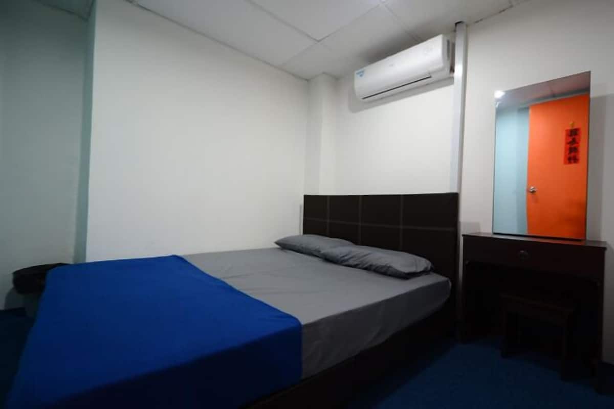 Uma cama de solteiro com edredom azul e cinza, cabeceira preta e um aparelho de ar condicionado acima.