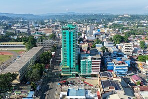 Um hotel moderno com vários andares, rodeado por uma área urbana densa com diversos edifícios e um campo esportivo.