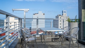 Terraço no telhado com mesa e cadeiras, vista para a paisagem urbana e para a água.