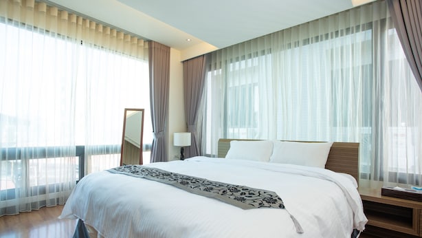 Quarto de hotel moderno com uma cama grande, uma mesinha de cabeceira, um espelho e cortinas leves.