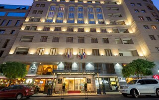 Um hotel com vários andares, uma entrada imponente, bandeiras e fachada bem iluminada.
