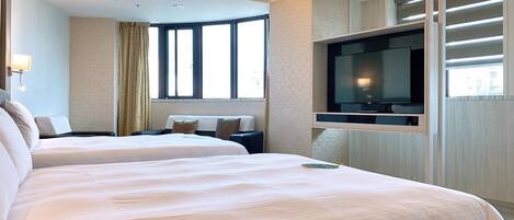 Quarto de hotel com duas camas, uma televisão e uma janela grande.