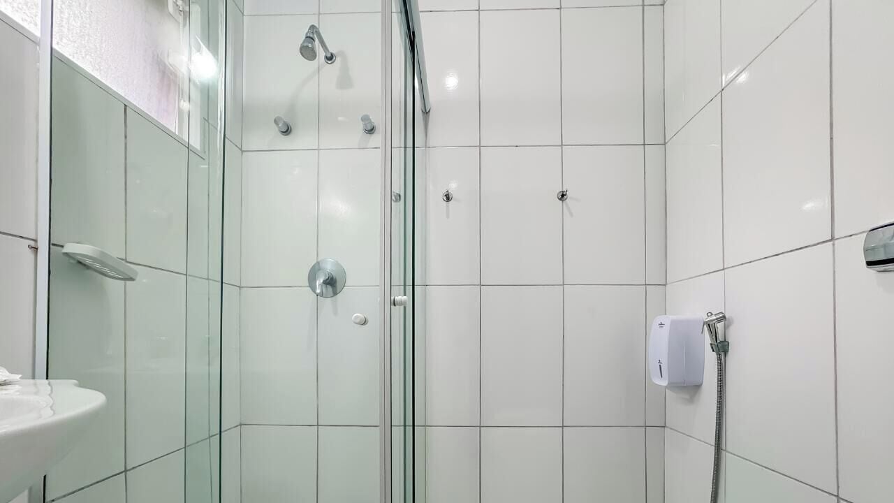Um banheiro moderno com box de vidro, pia branca e chuveiro manual.