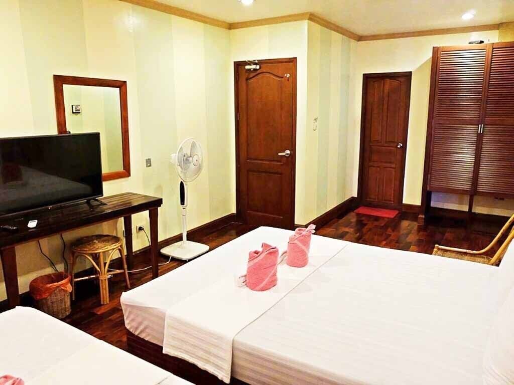 Quarto de hotel com uma cama, televisão, ventilador e portas de madeira.