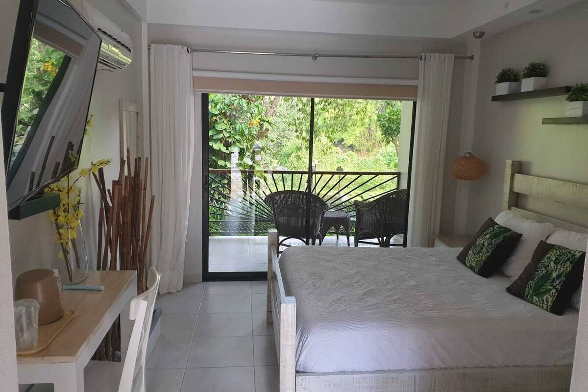 Quarto com cama, escrivaninha, cadeira e varanda com cadeiras.
