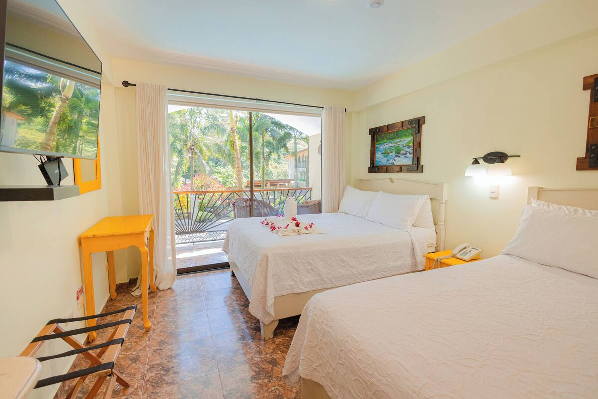 Quarto de hotel com duas camas, uma varanda, uma televisão e um quadro na parede.