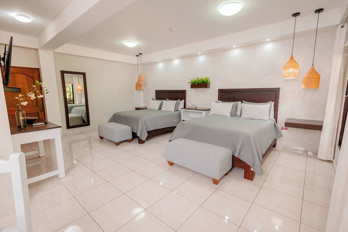Quarto de hotel com duas camas, uma mesa e uma televisão.