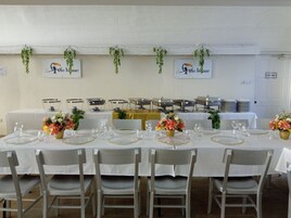 Salão de banquetes com mesas montadas para um evento formal, com toalhas brancas, pratos com detalhes dourados e arranjos florais.