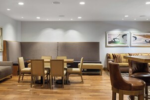Uma sala de jantar moderna com piso de madeira, uma mesa central com cadeiras e um sofá ao fundo.