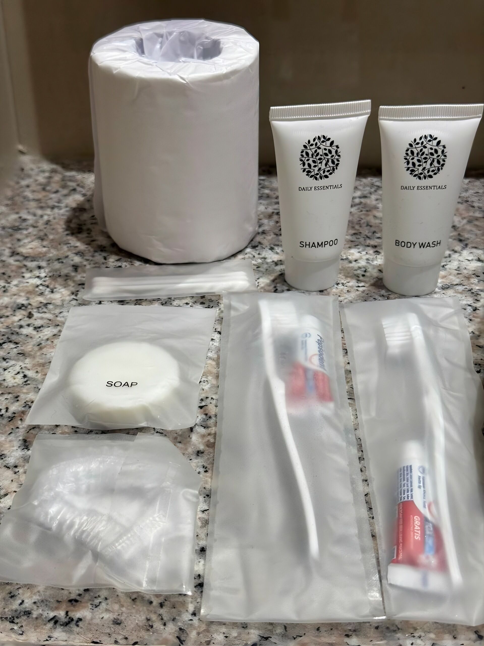 Artigos de higiene pessoal, incluindo um rolo de papel higiênico, dois frascos de shampoo, um sabonete em barra e uma escova de dentes.