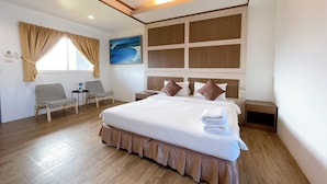 Quarto de hotel com uma cama grande, duas cadeiras, uma mesinha e um quadro na parede.