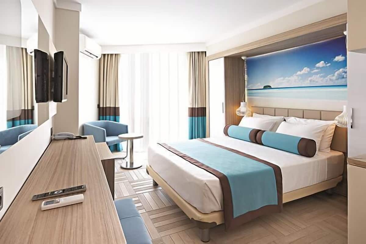 Quarto de hotel moderno com uma cama, uma escrivaninha, uma cadeira e uma grande janela com vista para o mar.