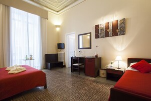 Quarto de hotel com duas camas, uma escrivaninha, uma cadeira, uma televisão, um espelho e um objeto decorativo na parede.