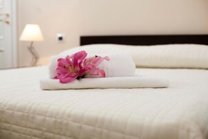 Cama bem arrumada com um edredom branco e uma flor rosa sobre uma toalha branca.