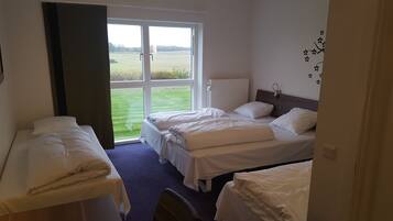 Quarto de hotel com duas camas de solteiro, uma janela grande com vista para um campo verde e uma luminária fixada na parede.