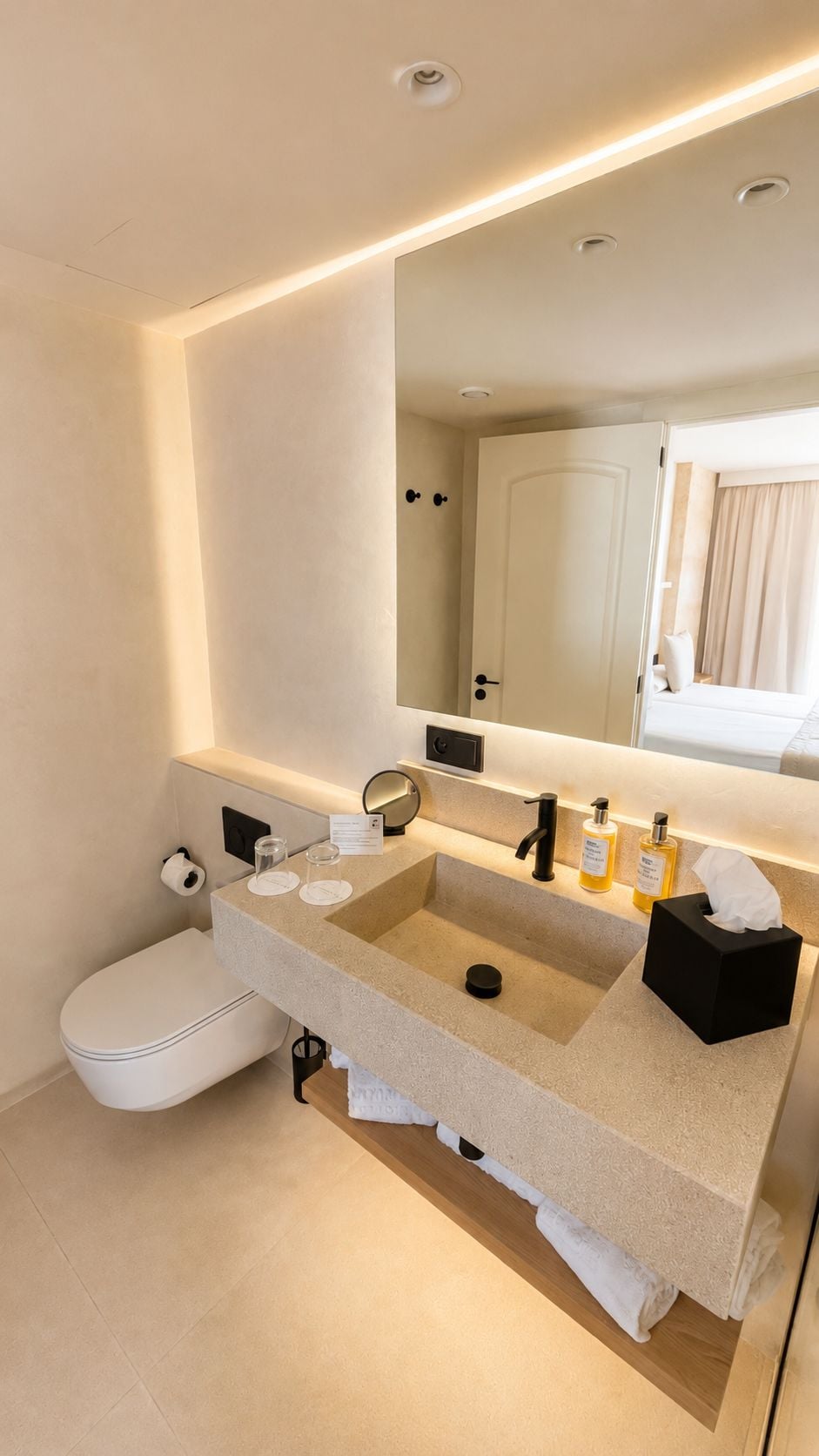 Uma casa de banho moderna com um espelho grande, uma sanita bege, uma sanita e um porta-toalhas.