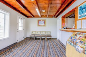 Um saguão de hotel com carpete estampado, vigas de madeira no teto, balcão de recepção com folhetos e um quadro emoldurado na parede.