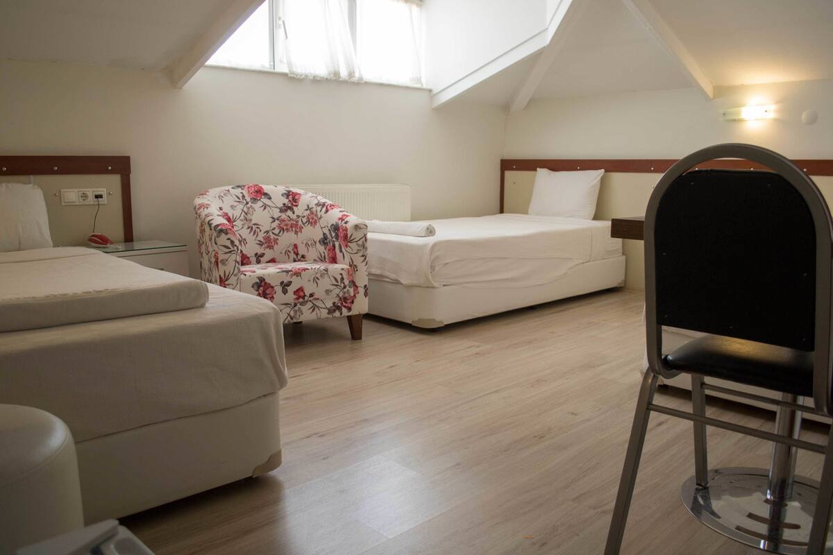 Quarto com duas camas, uma poltrona florida, uma cadeira preta e um claraboia.