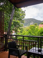 Área externa coberta com mesa e cadeira, com vista para uma paisagem verdejante e edifícios ao longe.