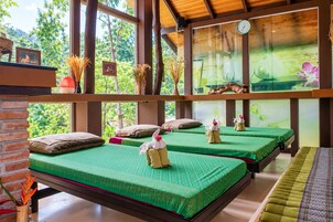 Quarto com três camas, cada uma com colcha e travesseiros verdes, e uma janela com vista para o verde.