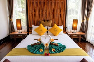 Quarto de hotel com uma cama grande, duas mesas de cabeceira com luminárias e uma cabeceira de madeira.