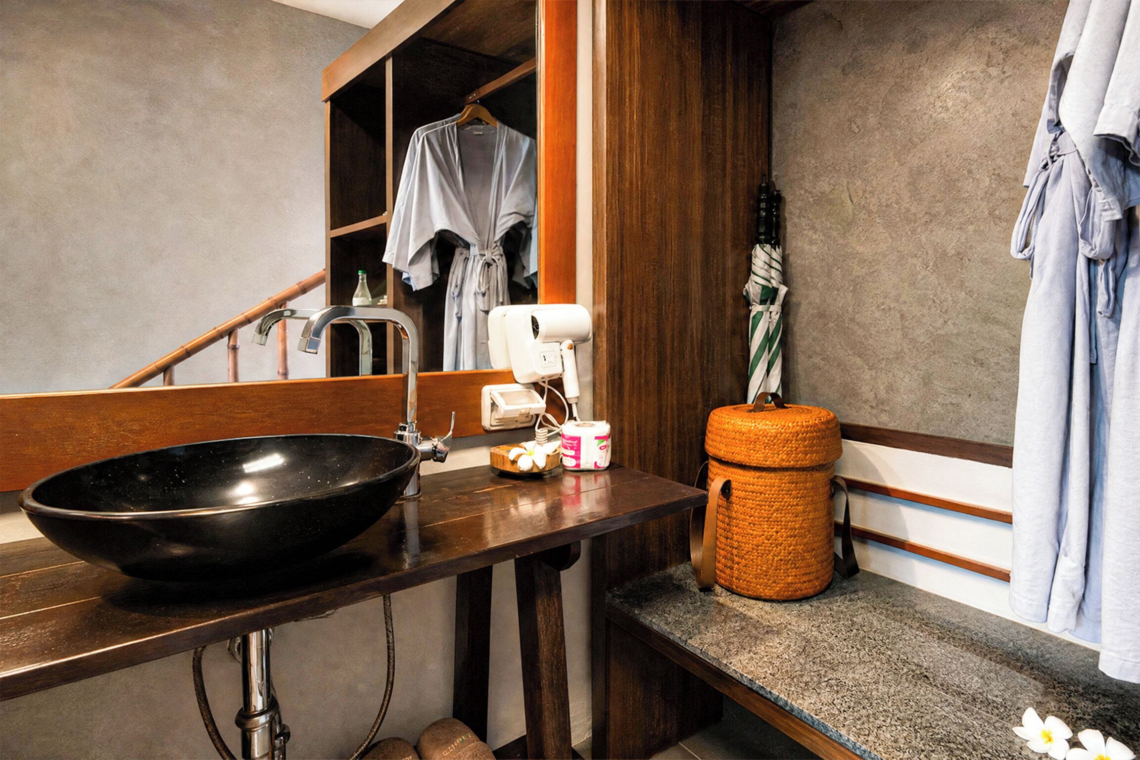 Casa de banho com lavatório preto, dispensador de toalhas e cesta de vime no balcão.