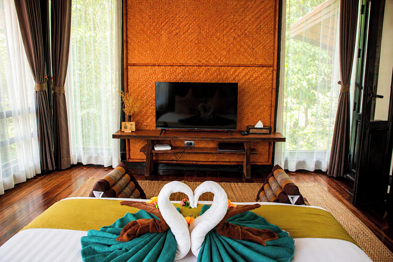 Quarto de hotel com cama, televisão e vista para o verde lá fora.