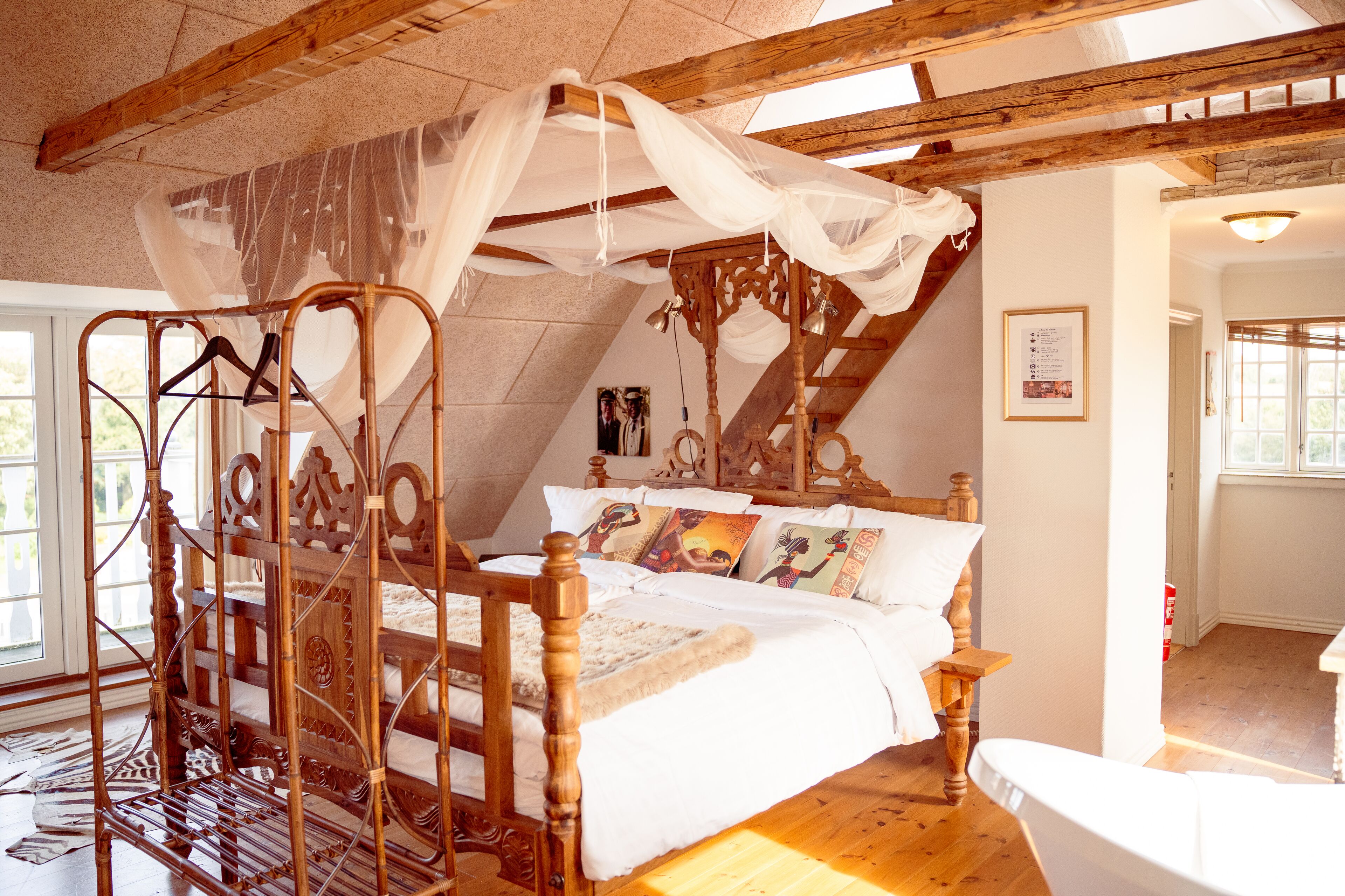 Quarto com cama de dossel de madeira, um toldo branco e vista para uma varanda.