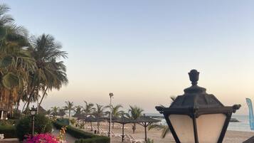 Um calçadão à beira-mar com flores vibrantes, palmeiras e guarda-sóis de praia.