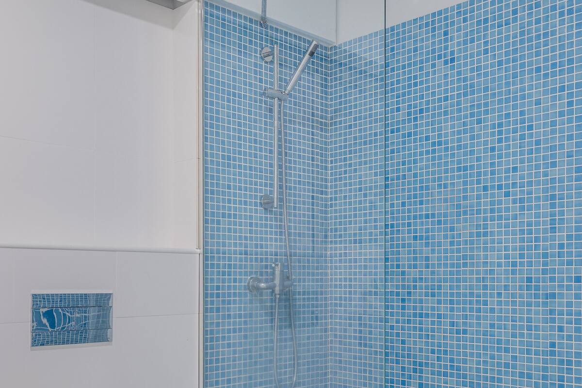 Um banheiro moderno com chuveiro em box de vidro, vaso sanitário branco e paredes azulejadas em azul.